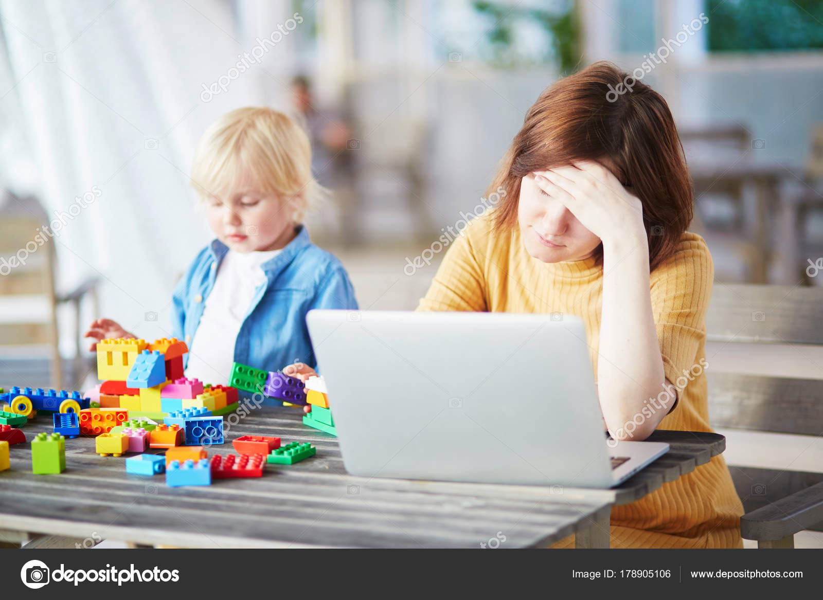 Little boy playing with construction blocks while his mother working on ...