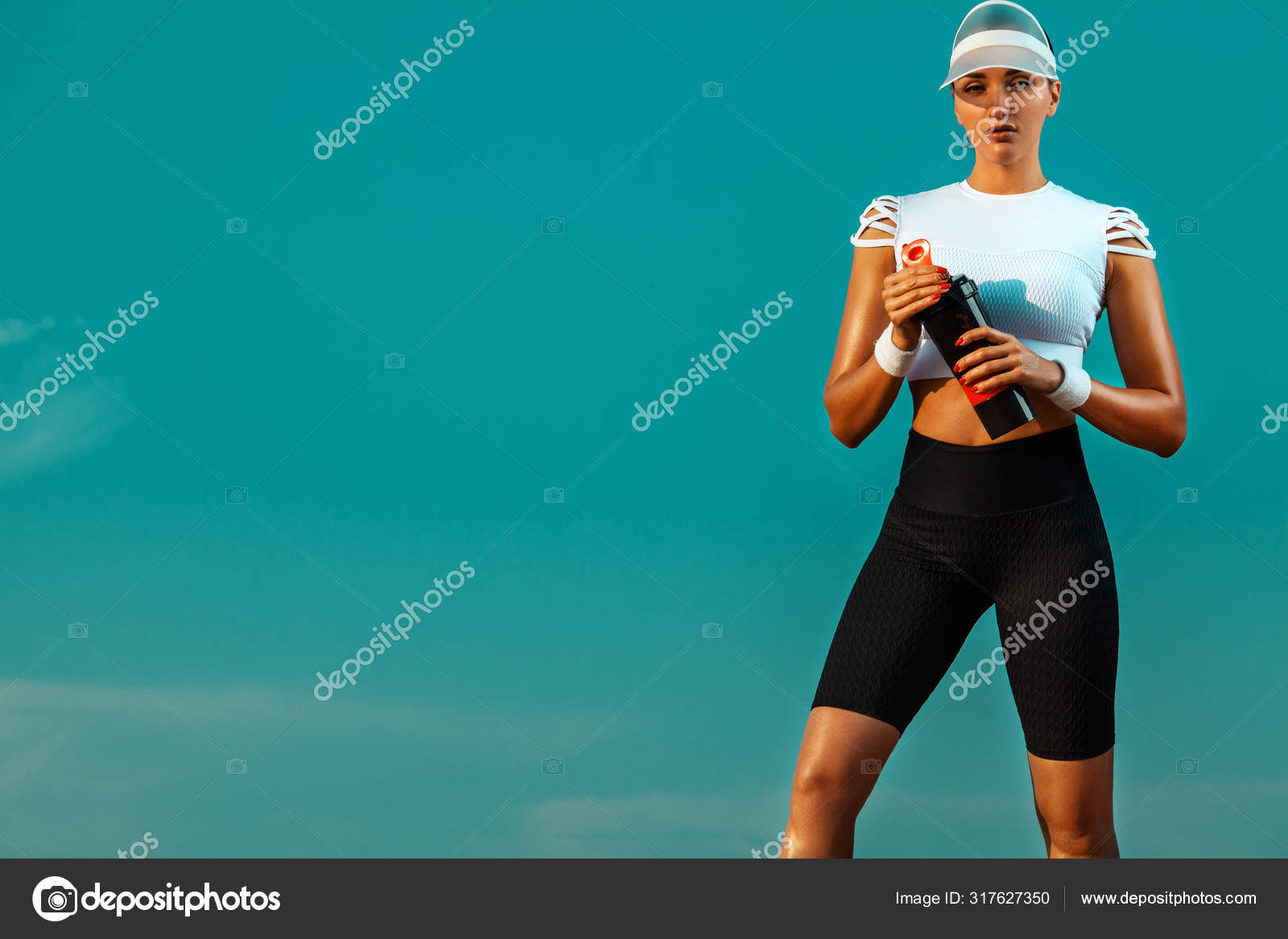 Female runner standing outdoors holding water bottle. Woman taking a ...