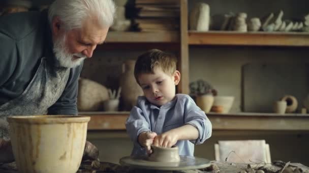 Diligent young learner is shaping clay pot under the guidance of his ...