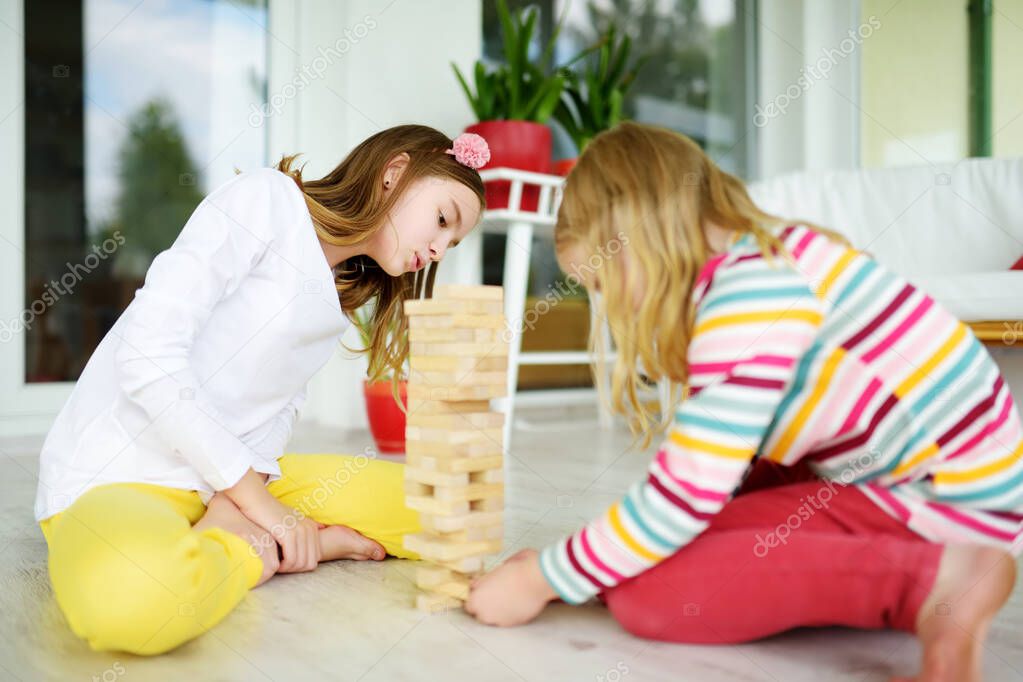 Dos hermanas lindas jugando bloques de madera juego de torre en casa. Niños practicando sus ...