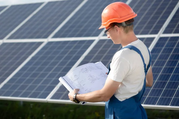 Young worker standing at solar energy station in the field. Stock Photo ...