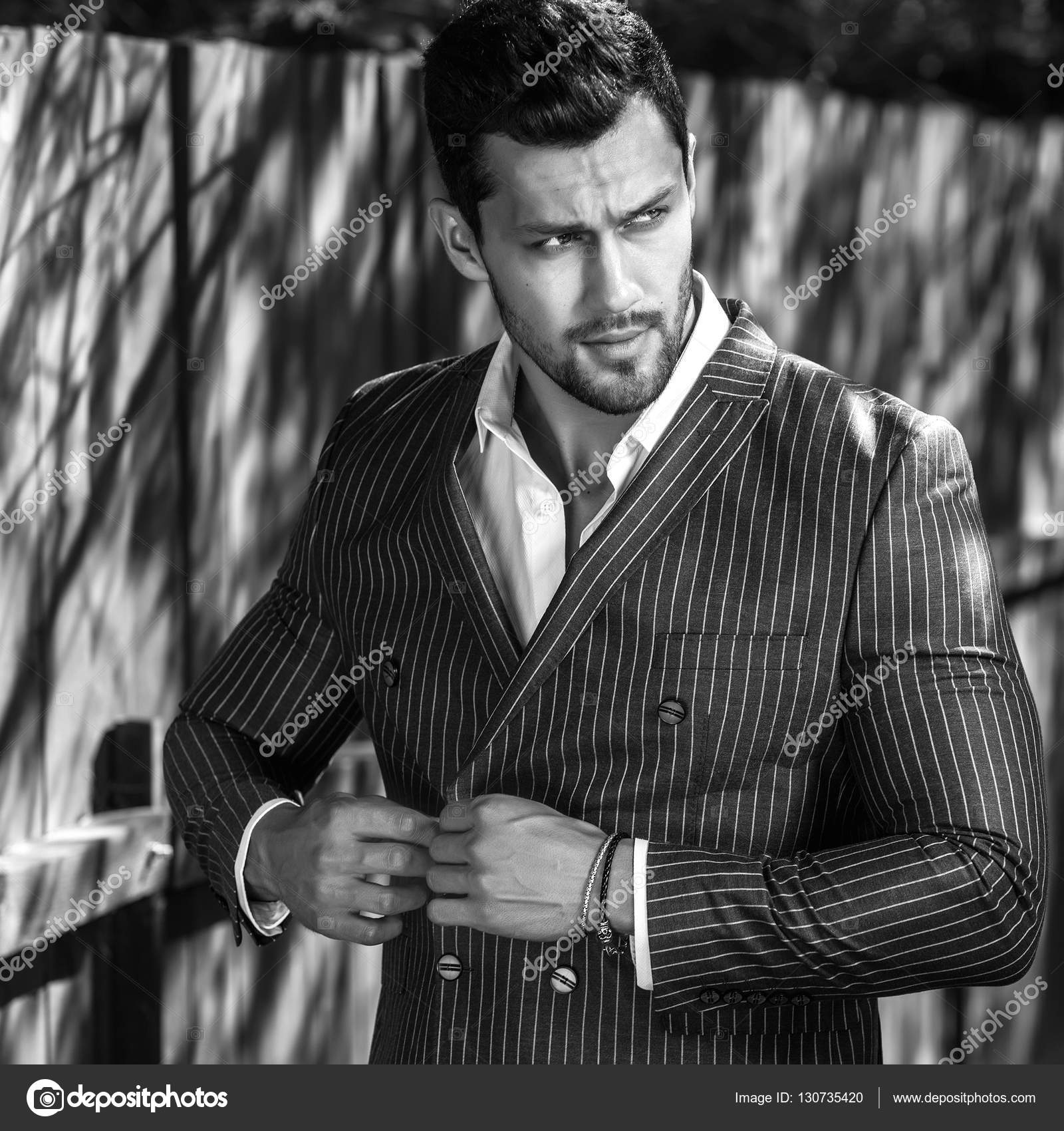 Elegant Handsome Man In Classical Grey Suit Poses Near Wooden Fence