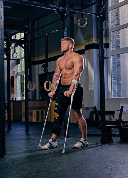 Bodybuilder on crutches holds dumbbell. Stock Photo by ©fxquadro 158611328