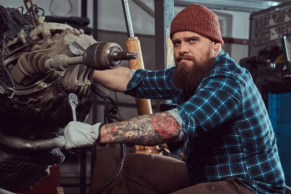 A brutal tattooed bearded mechanic specialist repairs the car engine ...
