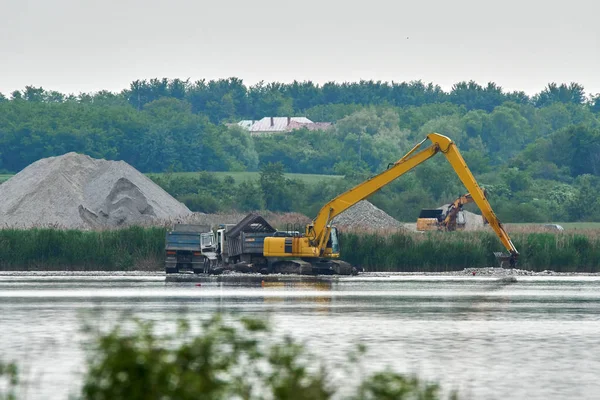 Excavator loading a truck on a lake - Stock Image - Everypixel
