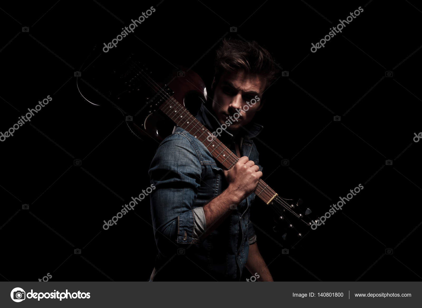 Dramatic young guitarist looking back while holding guitar on sh Stock ...