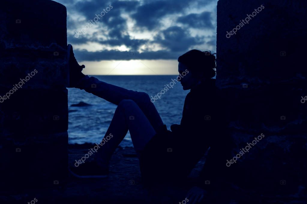 Silueta de una joven contemplando sentada en una pared sobre 2022