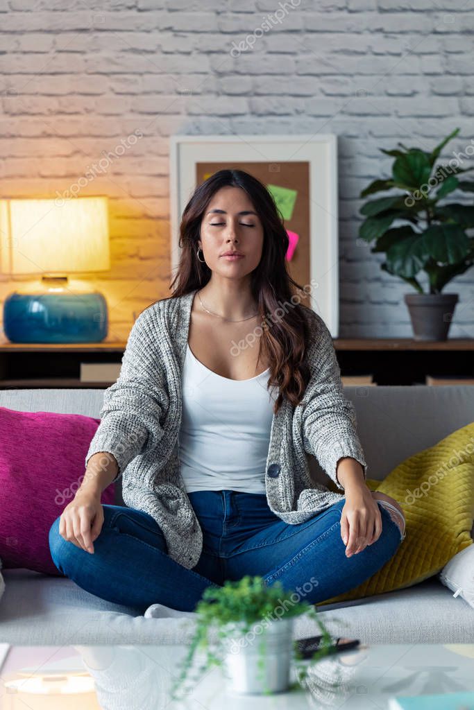 Mujer joven y bonita en posición de loto sentada en el sofá mientras se relaja en casa. 2023