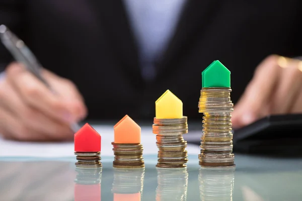 Businessperson Calculating Expenses In Front Of House Models On Top Of ...