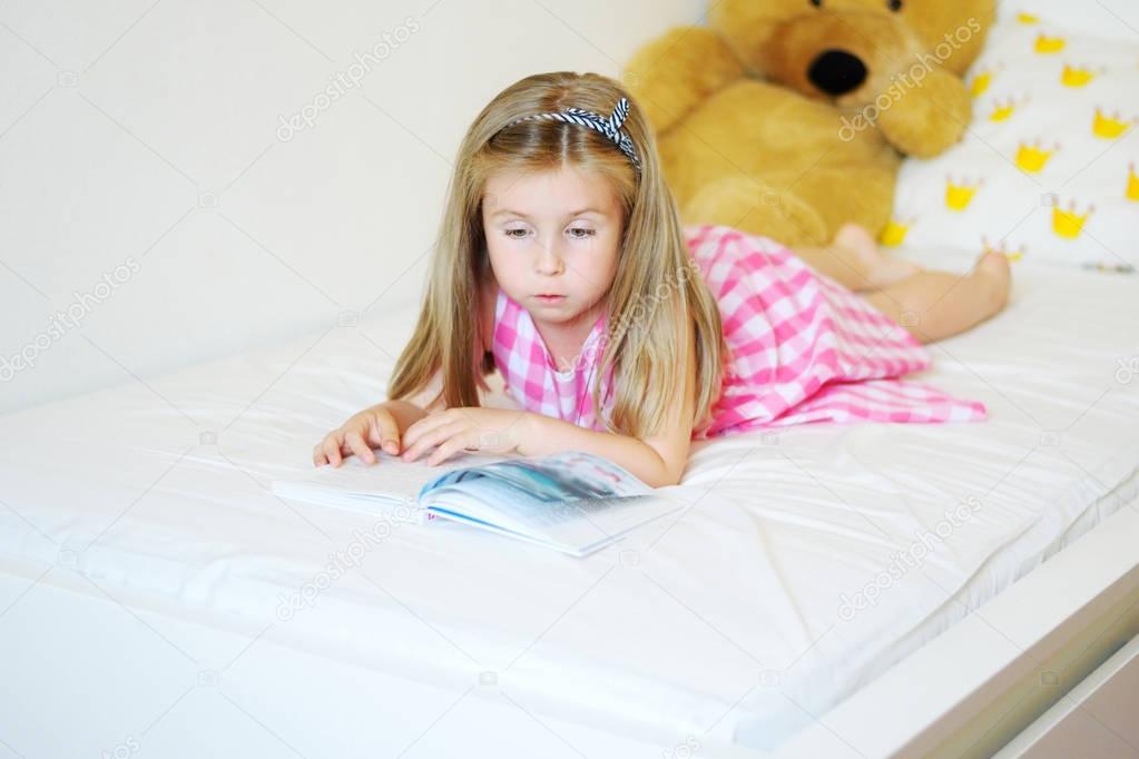 Adorable petite fille allongée sur le lit et lisant un livre image ...