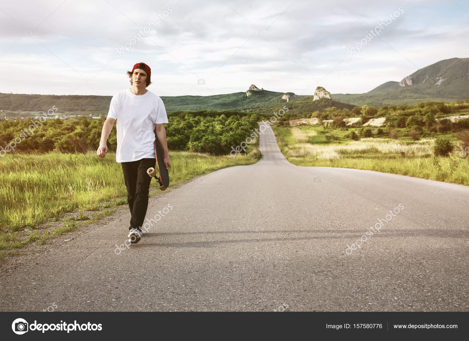 A man in a cap and with a long board in his hands is walking on a ...