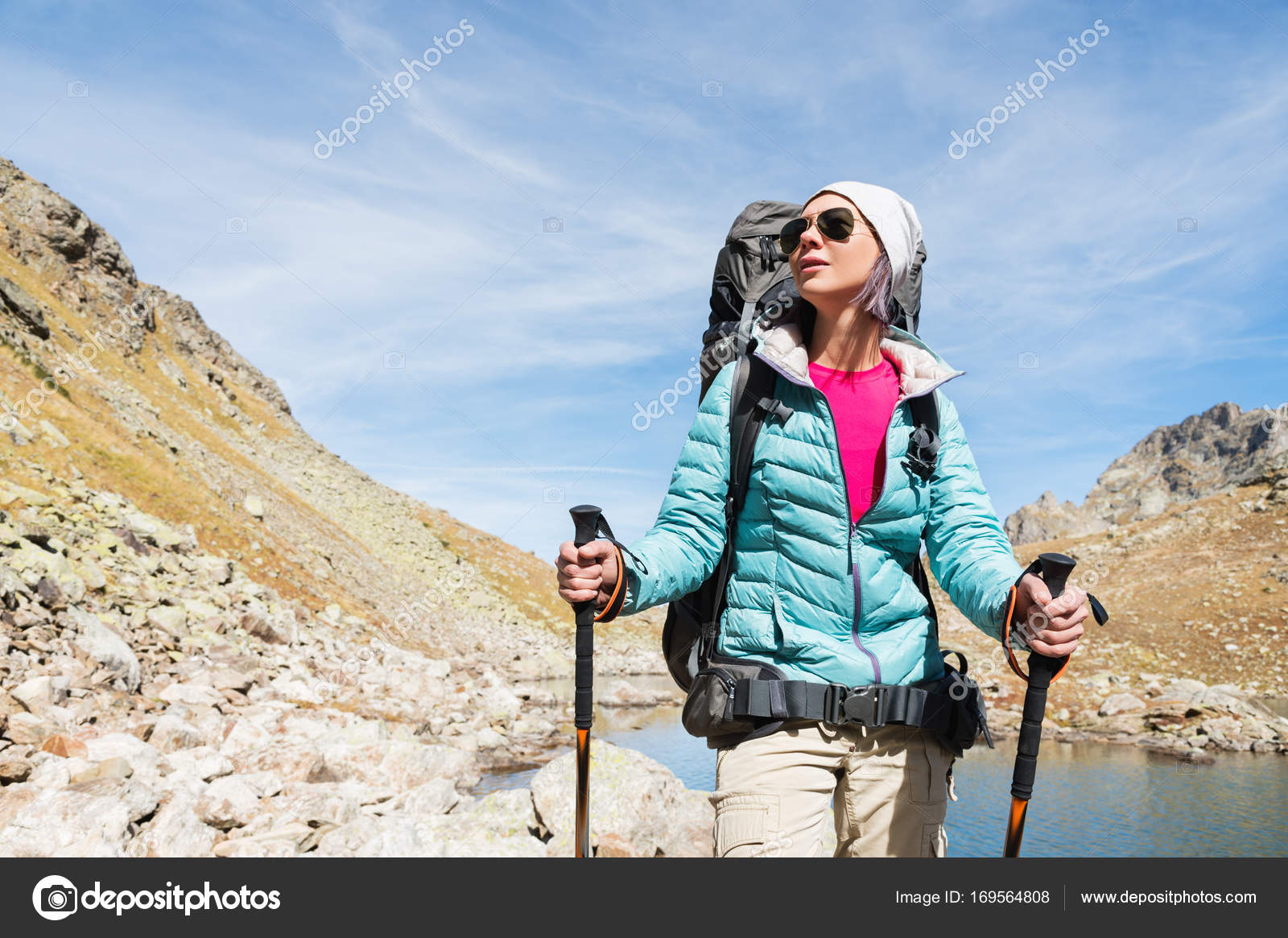 A hiker girl in sunglasses and a hat with a backpack and mountain gear ...