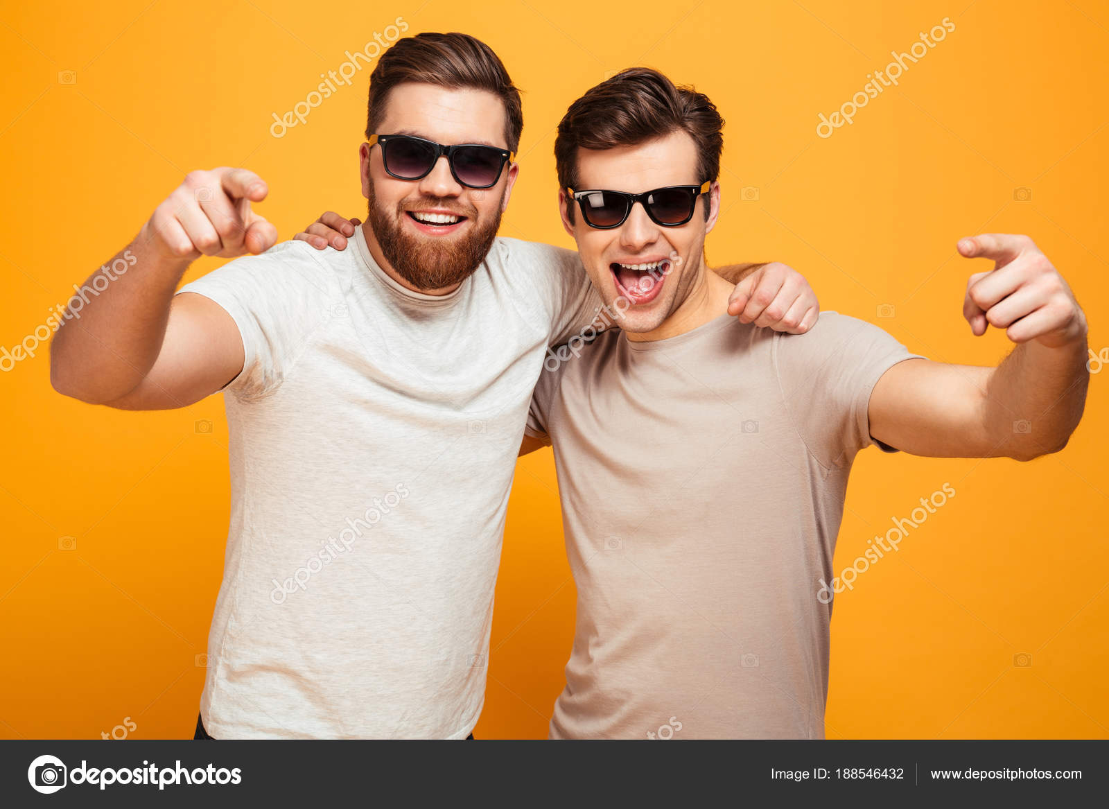 Two happy men in casual t-shirts and sunglasses hugging and poin ...