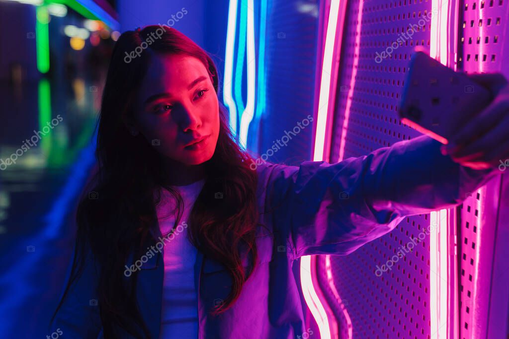 Hermosa joven mujer asi tica con el pelo largo y oscuro de pie delante de una pared de ne n 2024