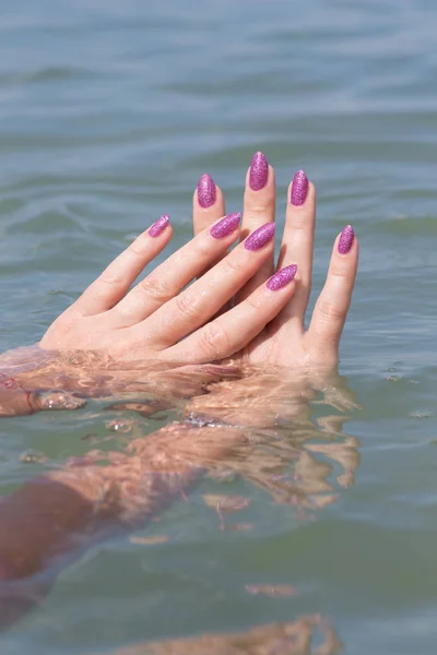 Female hands with pink nails in sea water and splashes - Stock Image ...
