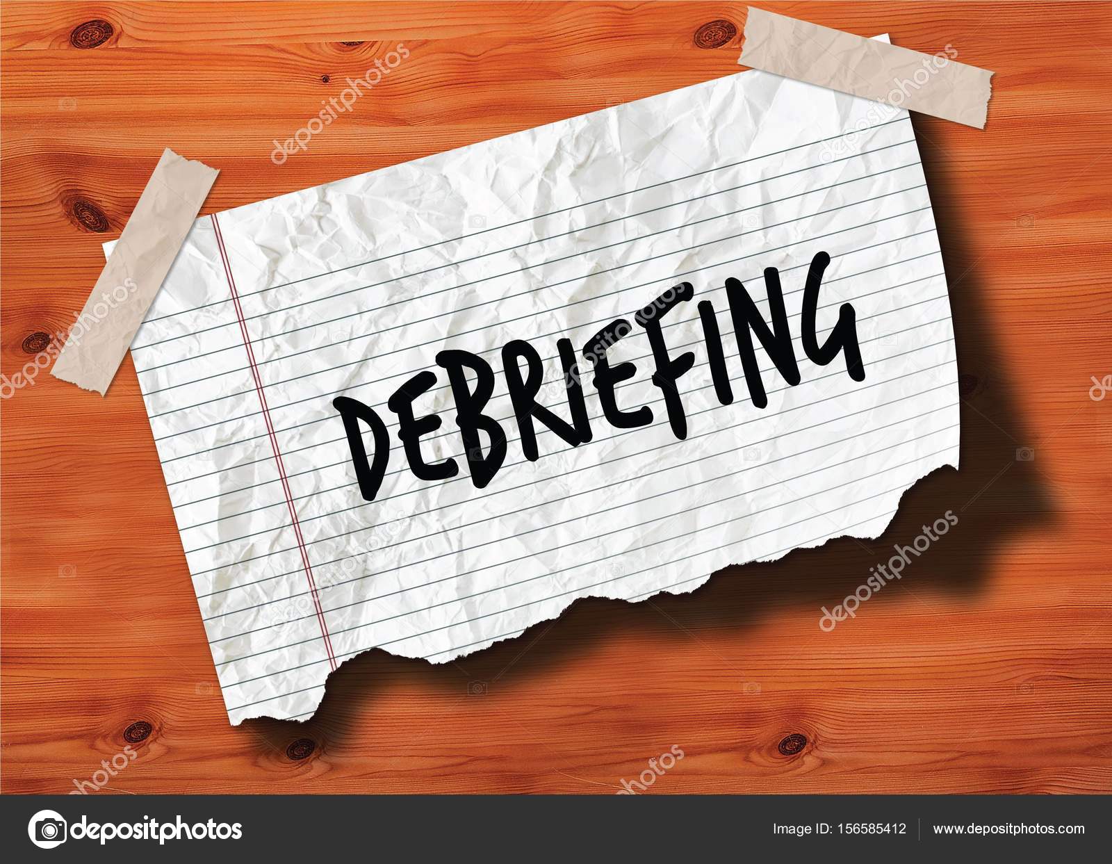 DEBRIEFING handwritten on torn notebook page crumpled paper on wood ...
