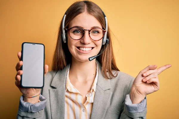 Young redhead call center agent woman using headset holding showing ...