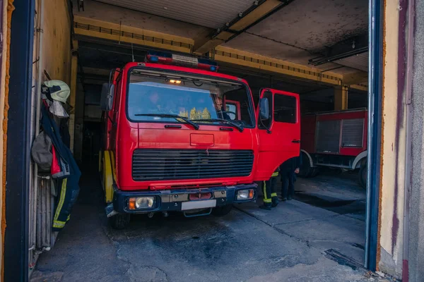 Young fireman holding a jacket and protective helmet in a garage of a ...
