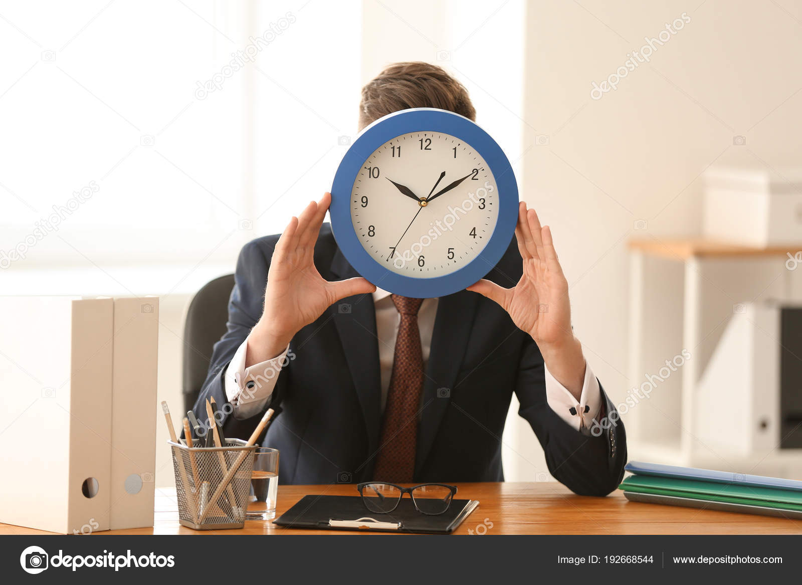 Man hiding face behind clock at table in office. Time management ...