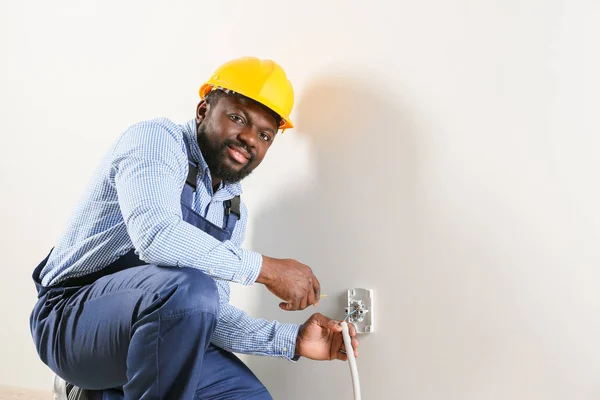 African-American electrician performing wiring in distribution board ...
