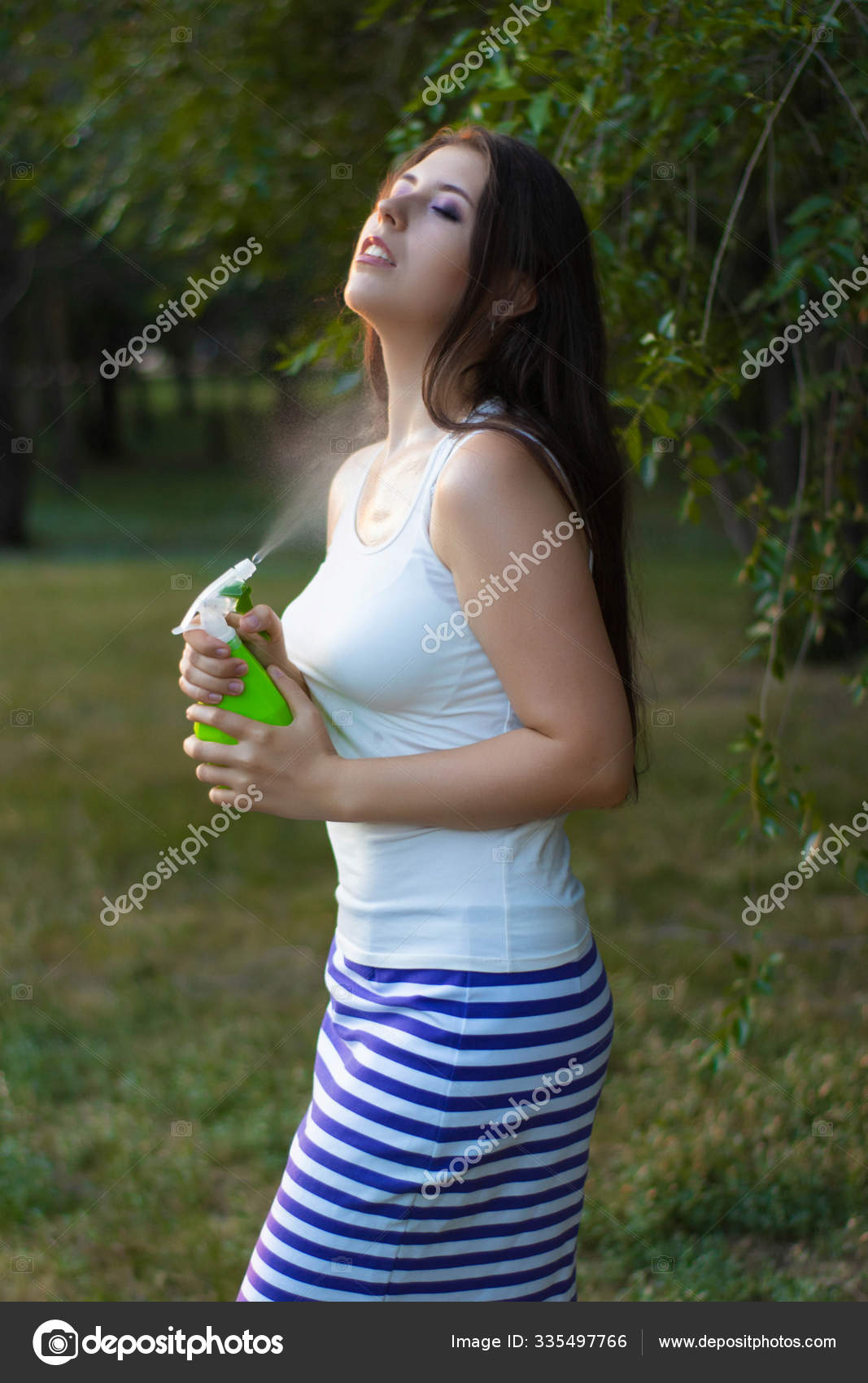 Young woman spraying water on herself from a spray bottle in a summer ...