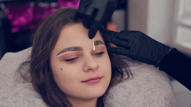 Professional woman eyebrow master handles a cotton bud with eyebrows to client in beauty salon ...