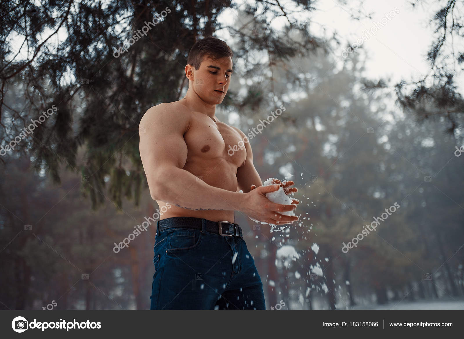 Young bodybuilder with bare torso wipes his body by snow in forest in ...