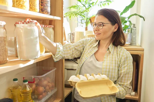 Woman in pantry taking flour, eggs. Food storage, cooking at home ...