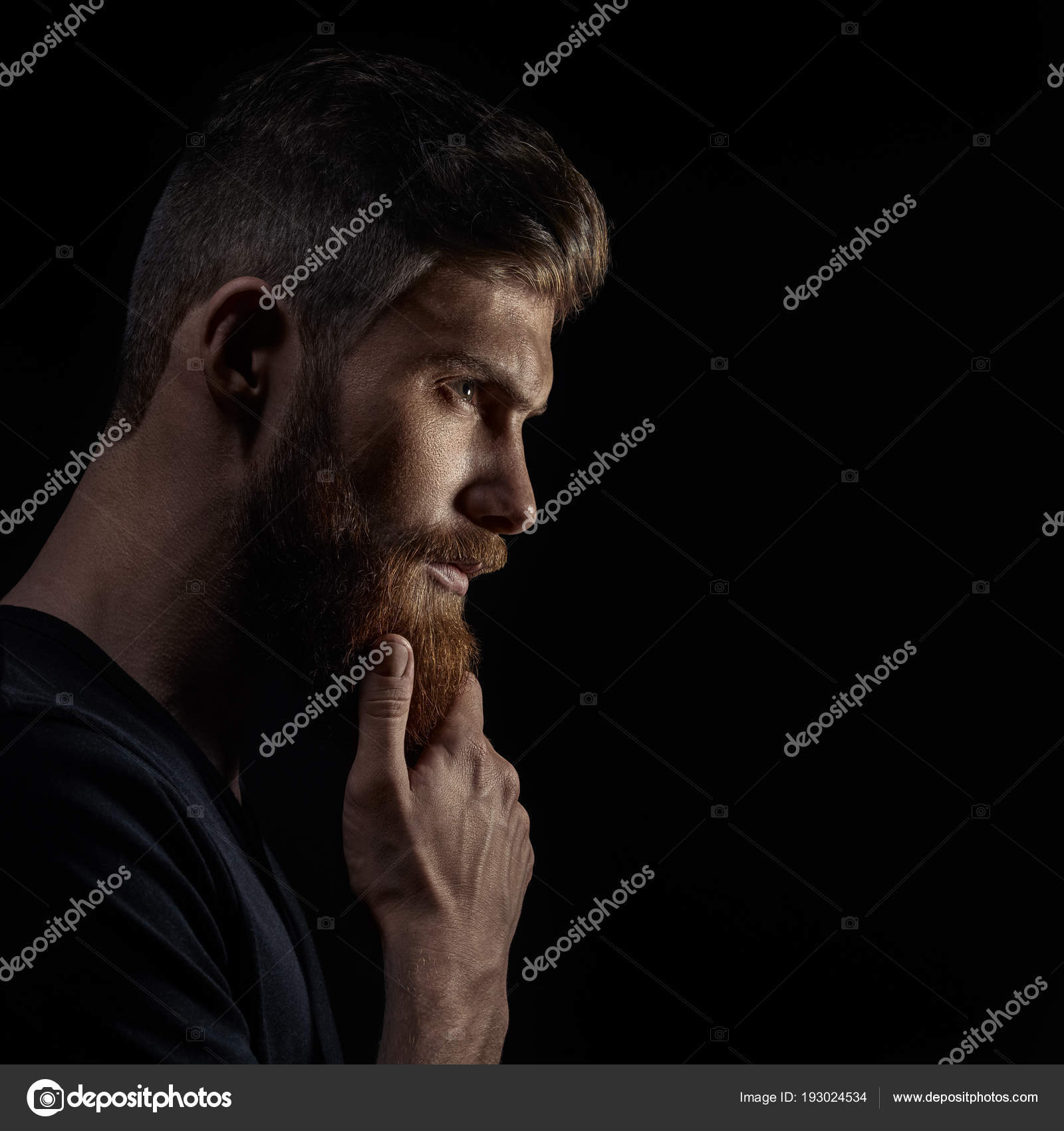 Attractive pensive young man looks into the distance stroking his beard ...