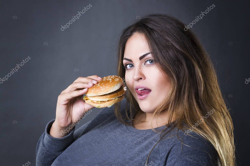 Happy beautiful young plus size model posing with hamburger on a gray ...