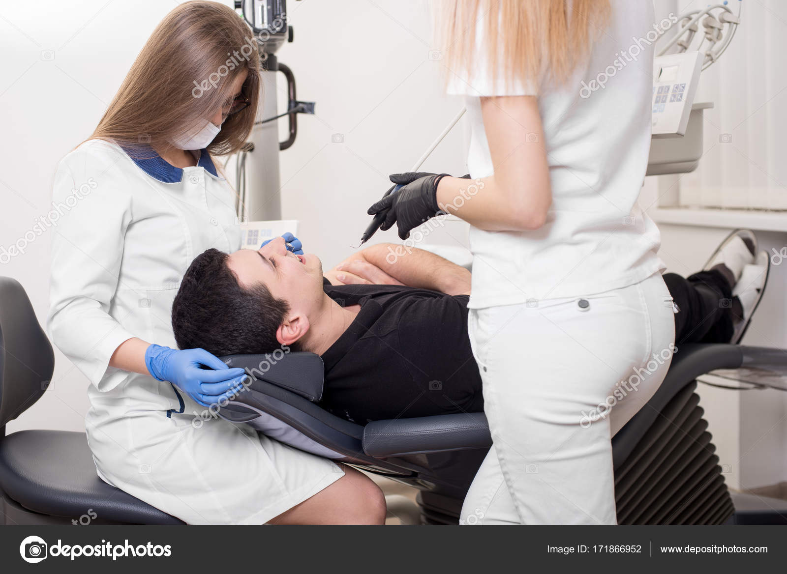 Two Female Dentists Treating Patient Teeth With Dental Tools At Dental