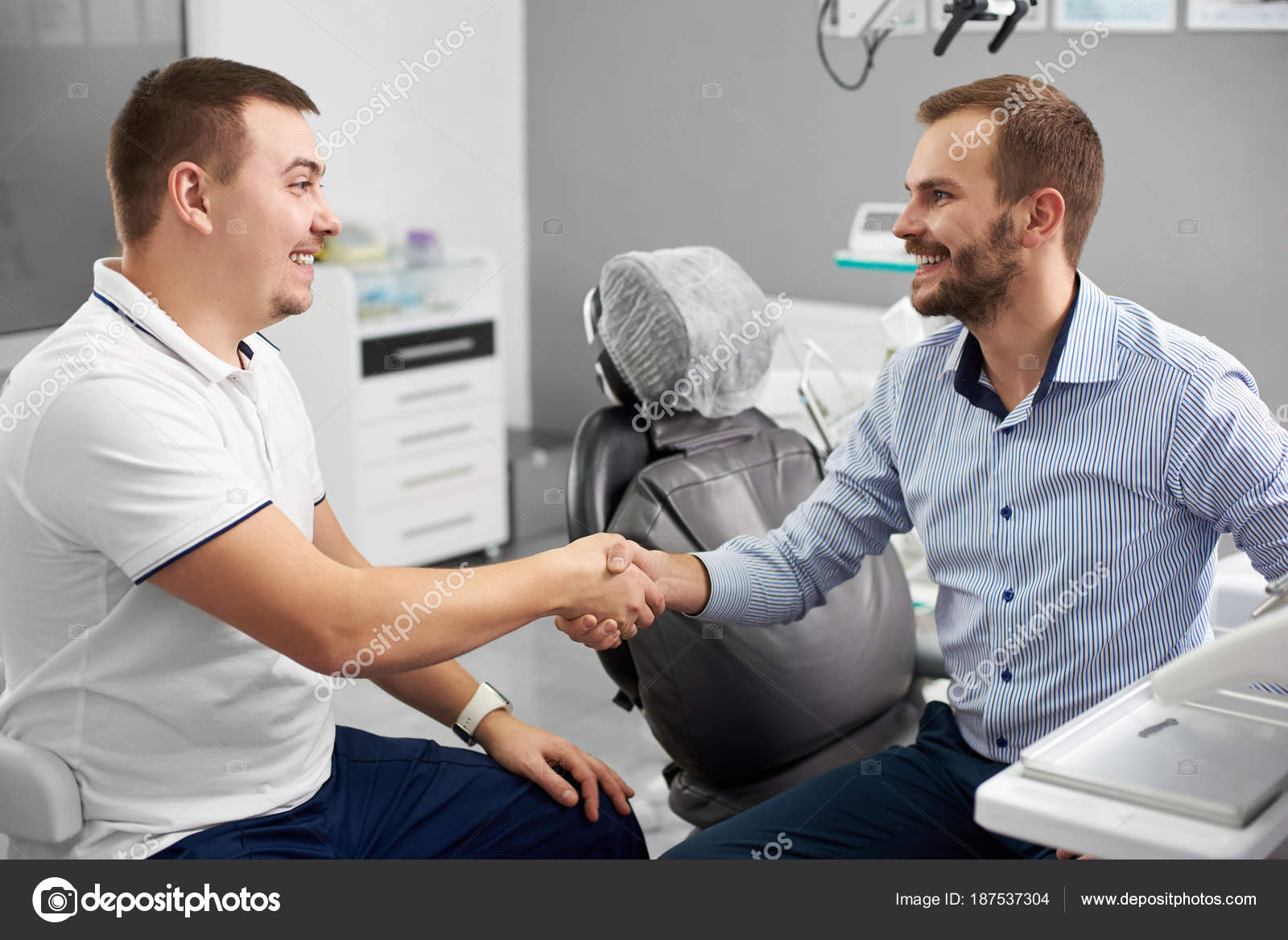 A young dentist and his attractive male client are shaking hands and ...