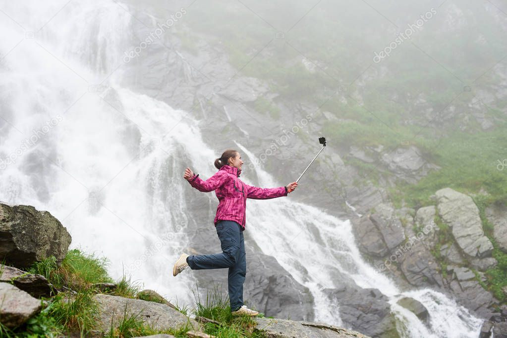 Sonriente joven hembra haciendo selfie posando en la roca frente a la ...