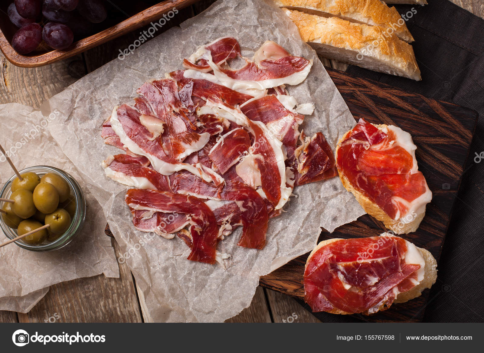 Jamon Iberico with white bread, olives on toothpicks and fruit on a ...