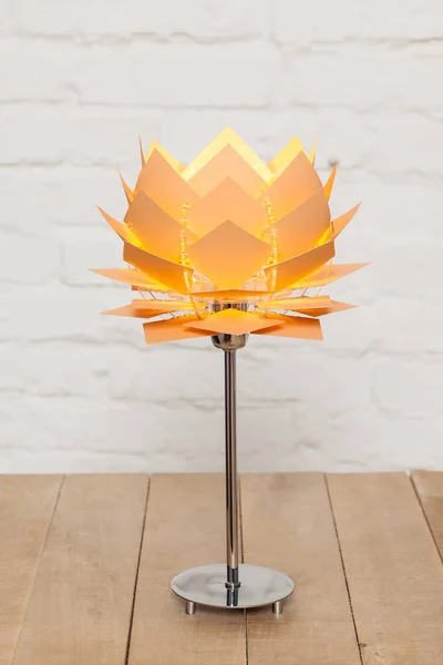 Front view of white conceptual table lamp on wooden stand on gray brick ...