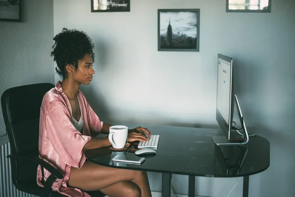 Black woman at home working with computer, smartphone and coffee in the ...