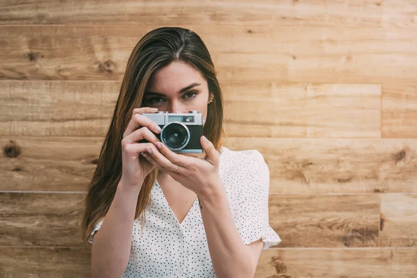 Beautiful woman with vintage old camera standing at a wood wall taking ...