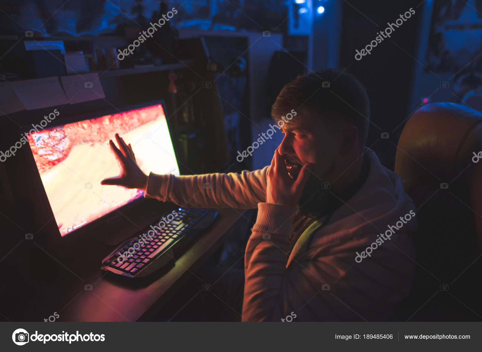 A frightened man sits at his computer at night and covers his ey ...