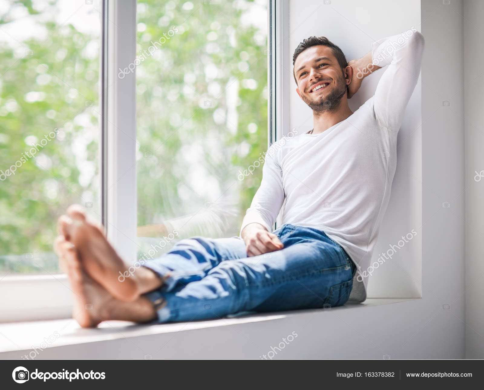 Handsome man relaxing on window sill Stock Photo by ©Gladkov 163378382