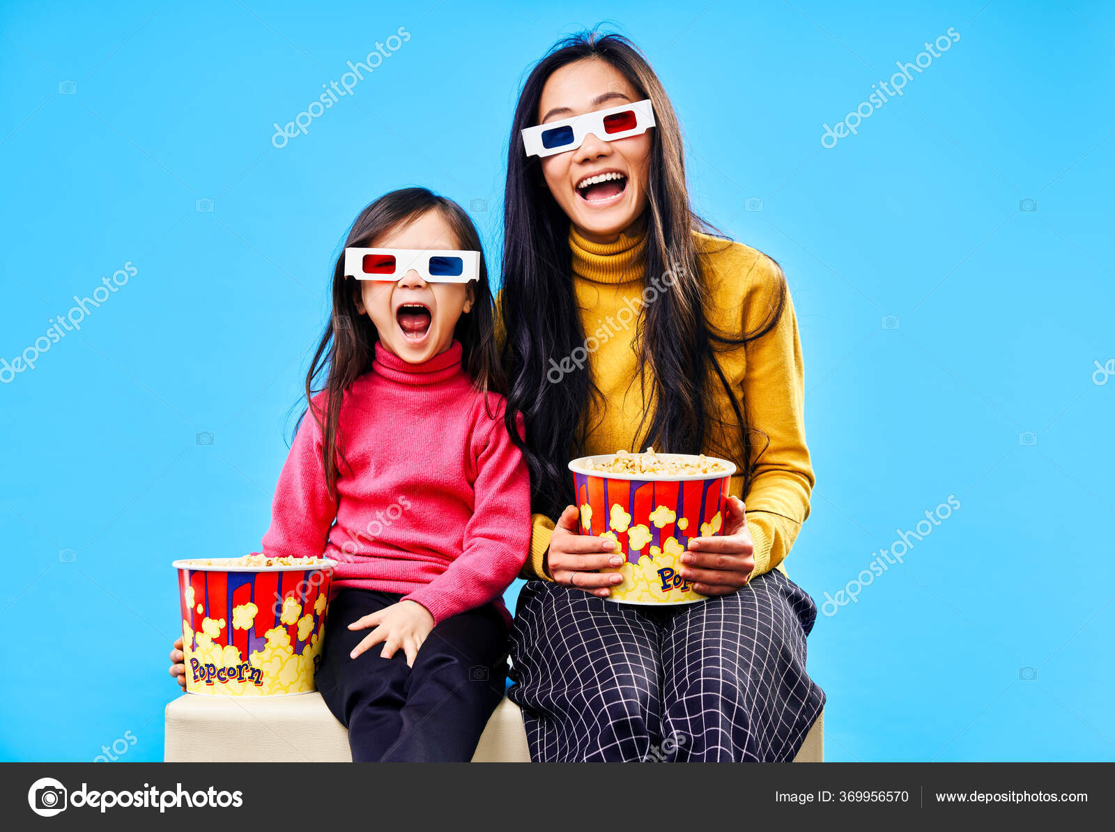 Surprised mother and her little daughter in 3D glasses with popcorn watching movie over blue ...