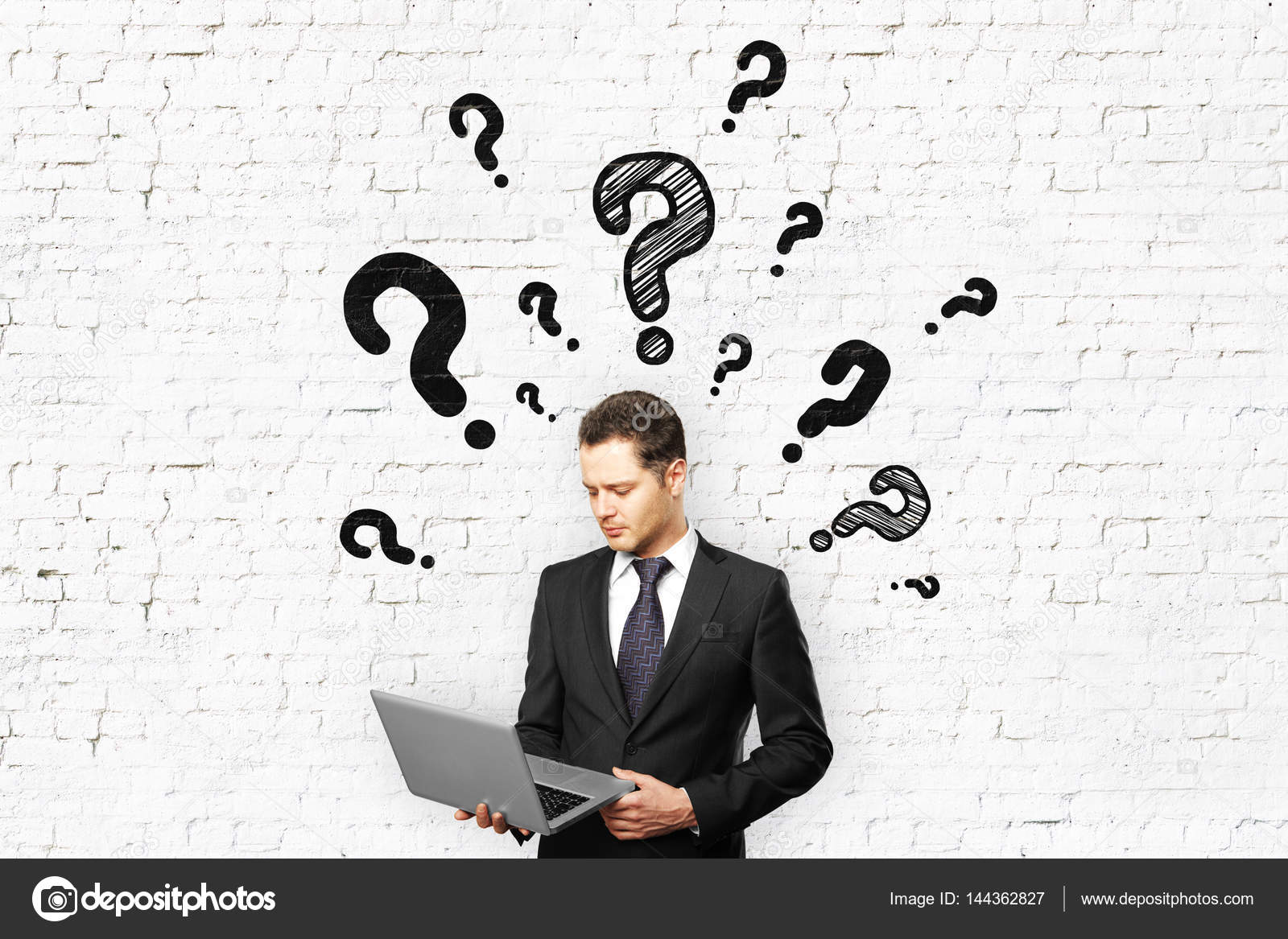 Businessman with laptop question marks on brick wall background ...