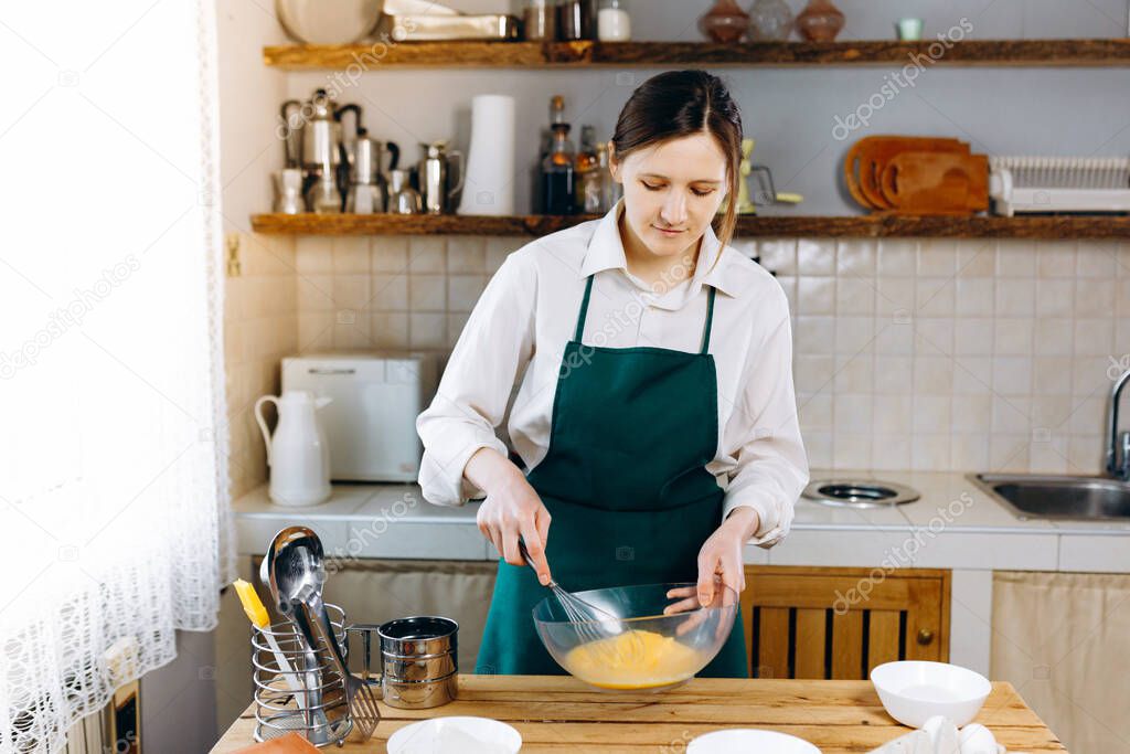Una joven feliz chica se para en la cocina en la mesa y va a hornear ...
