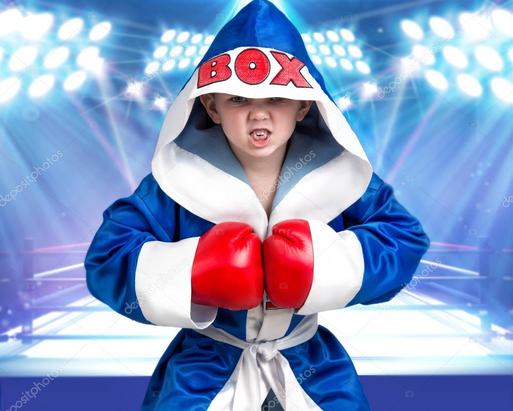 Little boy boxer with red gloves and robe in the background of the ring ...