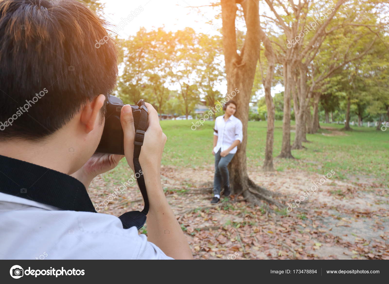 Back view of photographer taking a photo of young man in summer park ...
