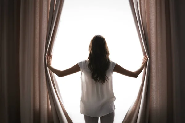 Beautiful woman opening curtains — Stock Photo © belchonock #138221028