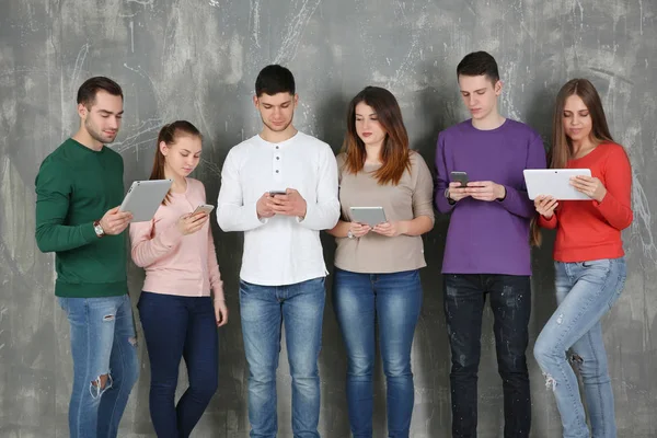Young people using digital devices on gray textured background - Stock ...