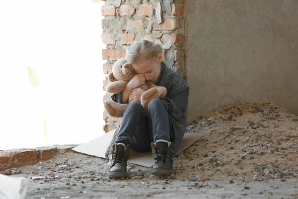 Poor, sad little child girl sitting against the concrete wall — Stock ...