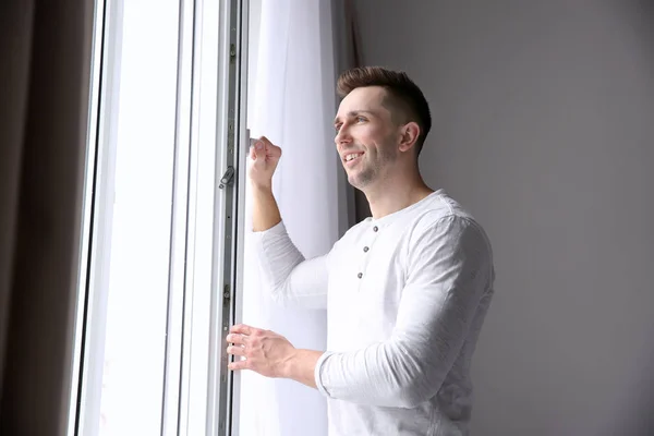 Smiling man opening window Stock Photo by ©belchonock 157996778