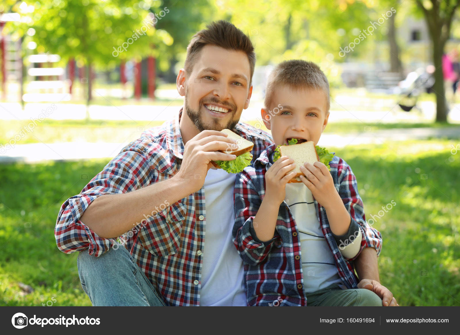 Dad and son eating lunch in the park on sunny day Stock Photo by ...