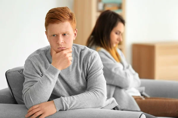 Quarrelled young couple sitting on sofa in light room - Stock Image ...